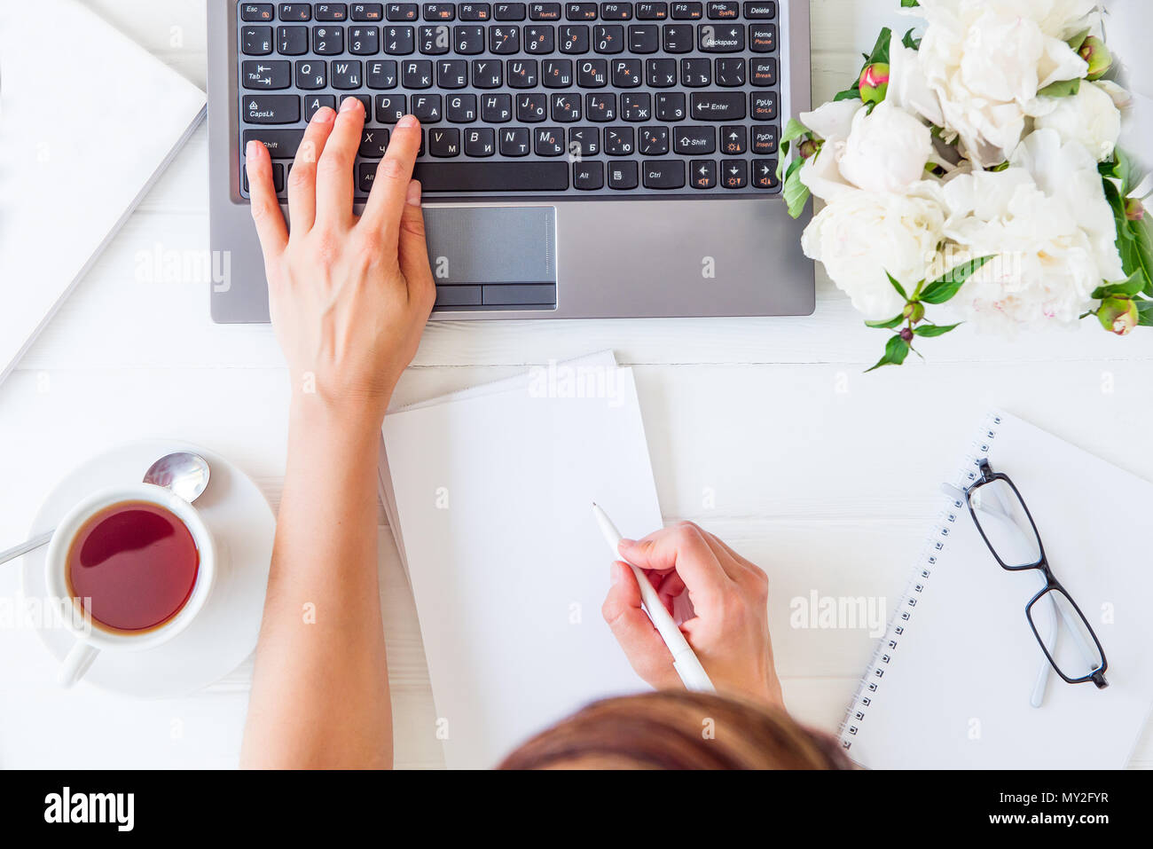 Workspace with girl's hand on laptop keyboard and writing in notebook ...