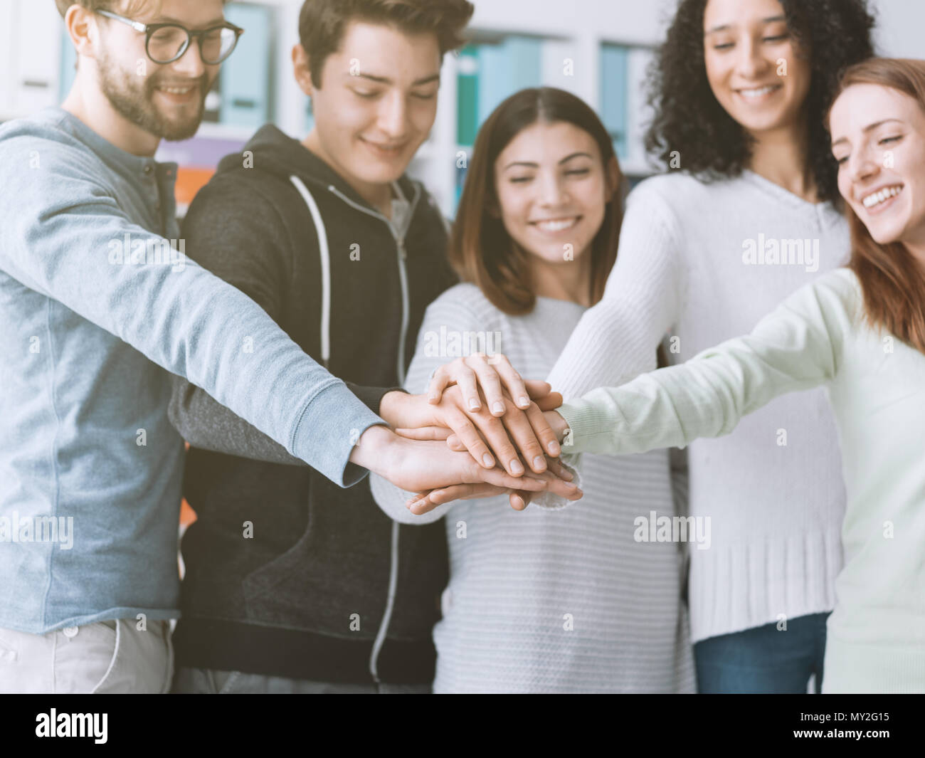 College students and friends stacking hands together and smiling ...
