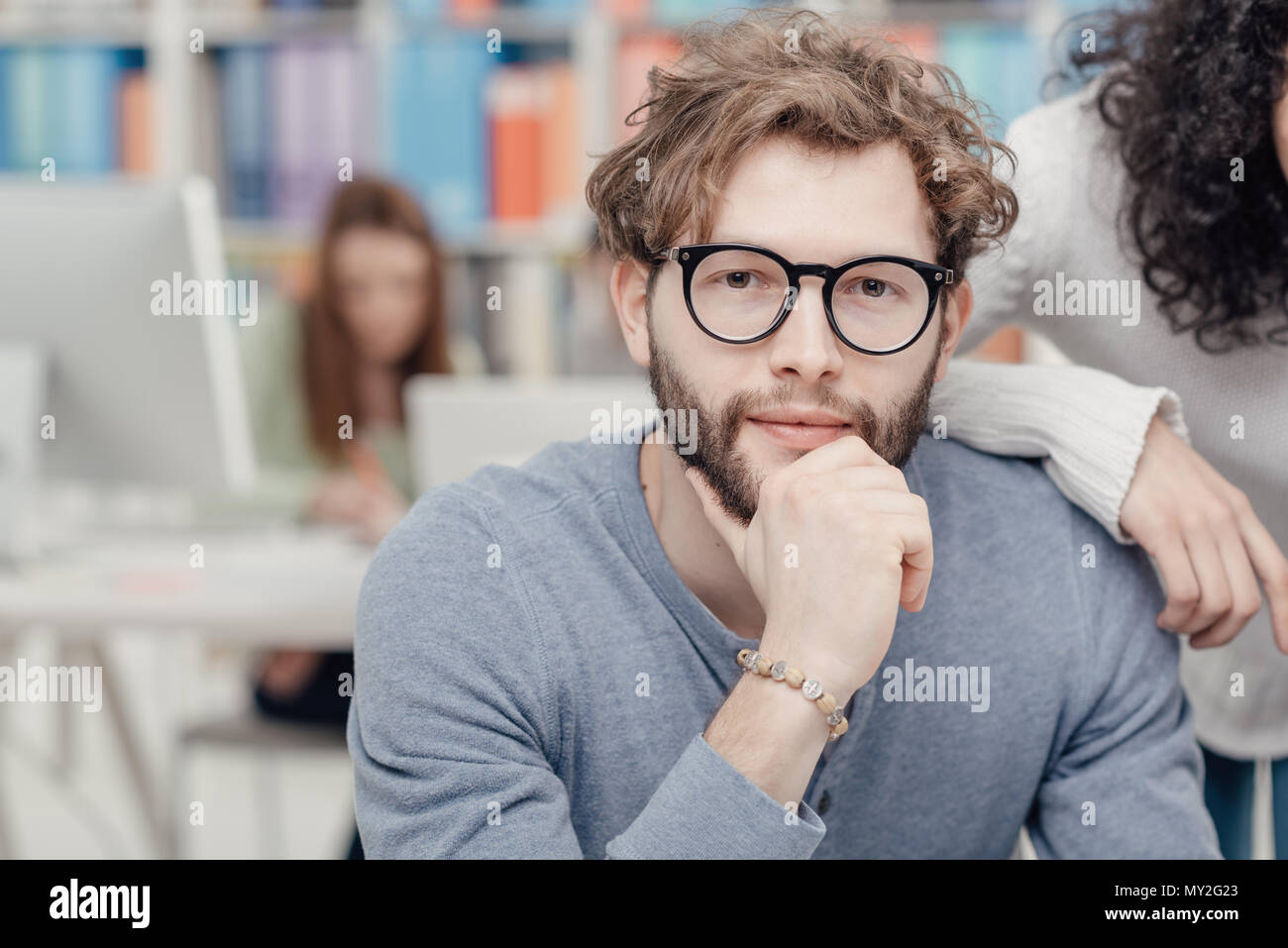Young smiling hipster man sitting at desk, his colleague is leaning on ...