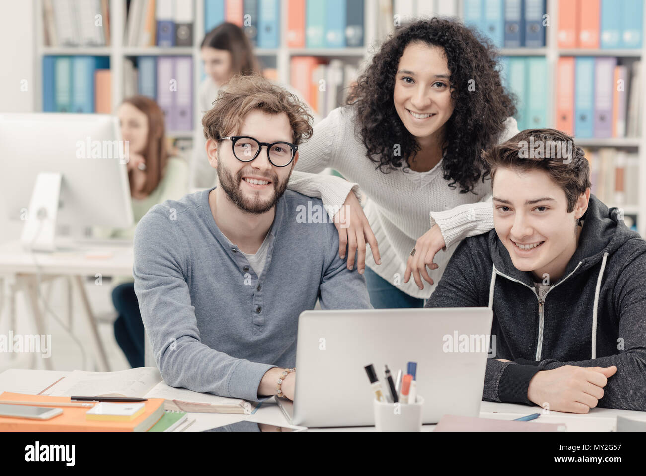 Group of happy students connecting together with a laptop and smiling ...