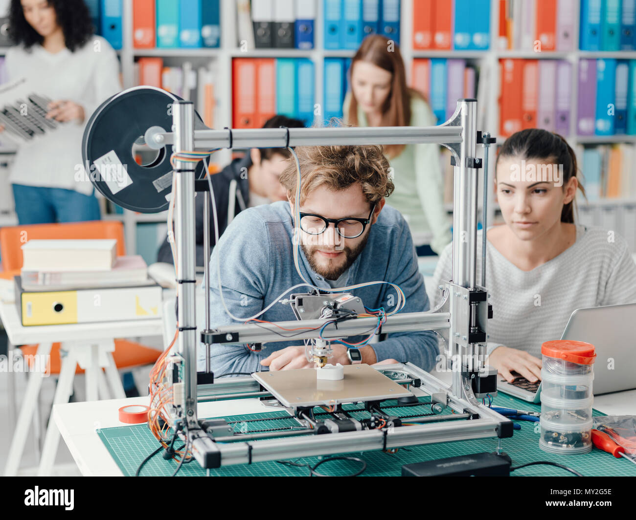 Male and female engineering students using a 3D printer in the lab ...