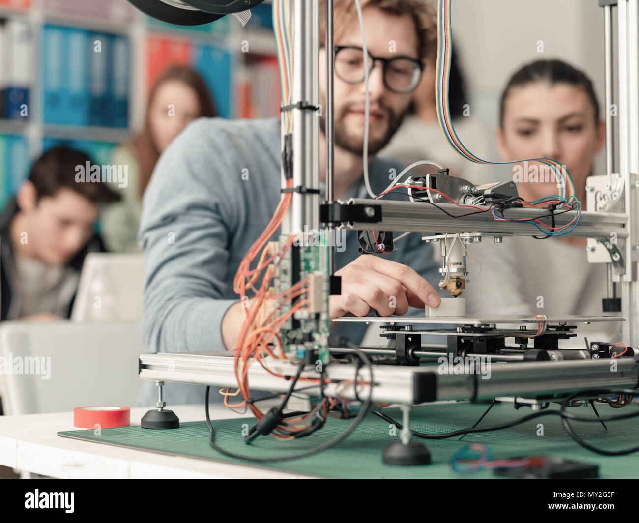 Male and female engineering students using a 3D printer in the lab ...