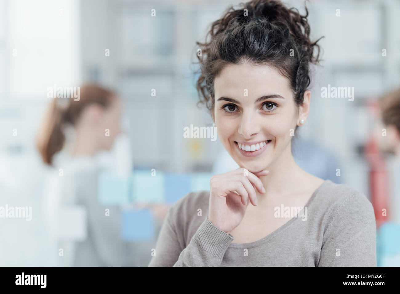 Young smiling female office worker posing, she is smiling at camera ...