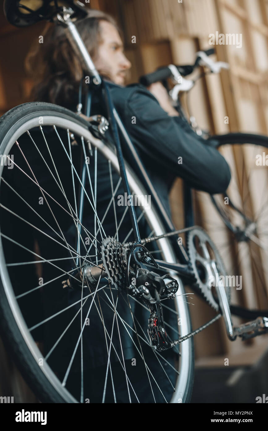 Close-up view of young man walking and carrying bicycle on shoulder ...