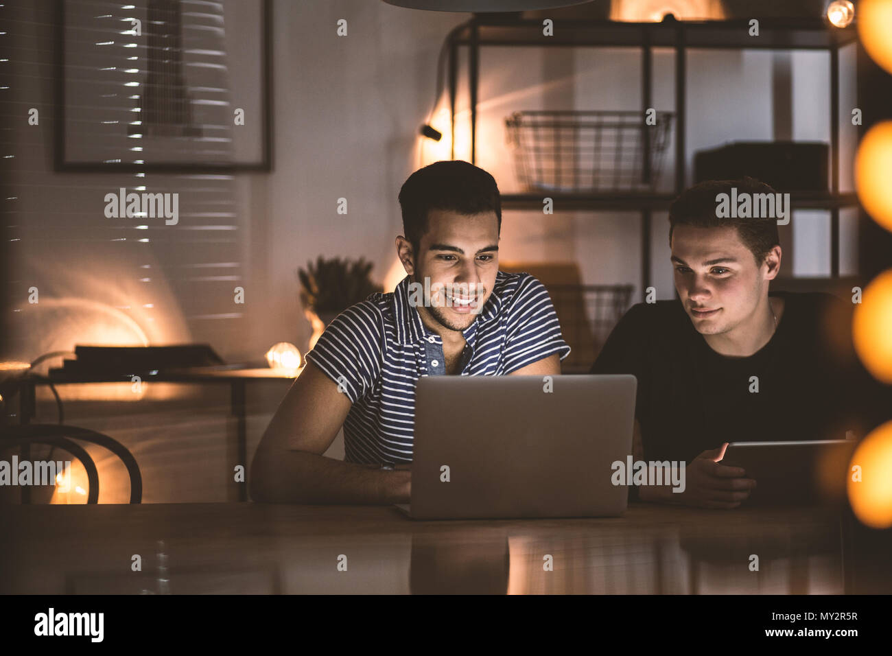 Young men sitting in front of a laptop at night with subtle lights ...