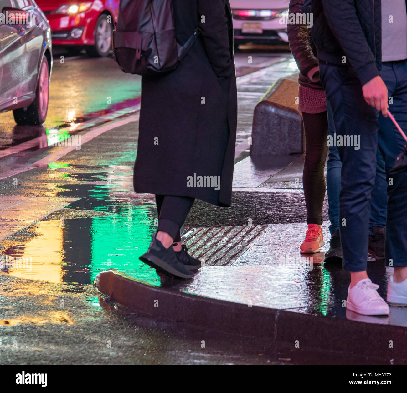 A woman walking through Times Square, New York City in rain with puddle ...