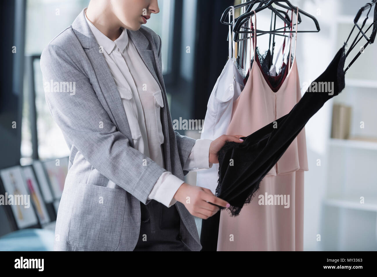 cropped shot of fashion designer examining quality of clothing on rack ...