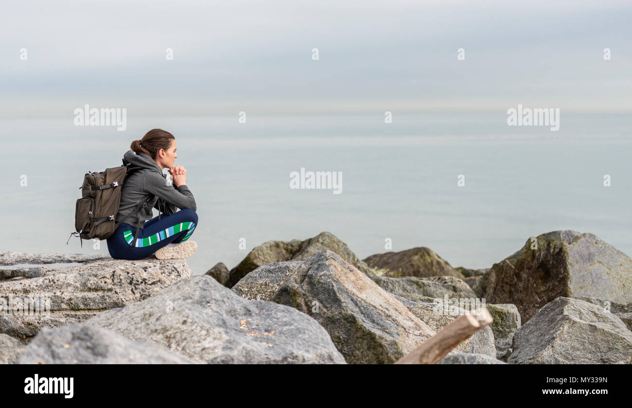 woman wearing a backpack sitting on rocks resting and enjoying the view ...