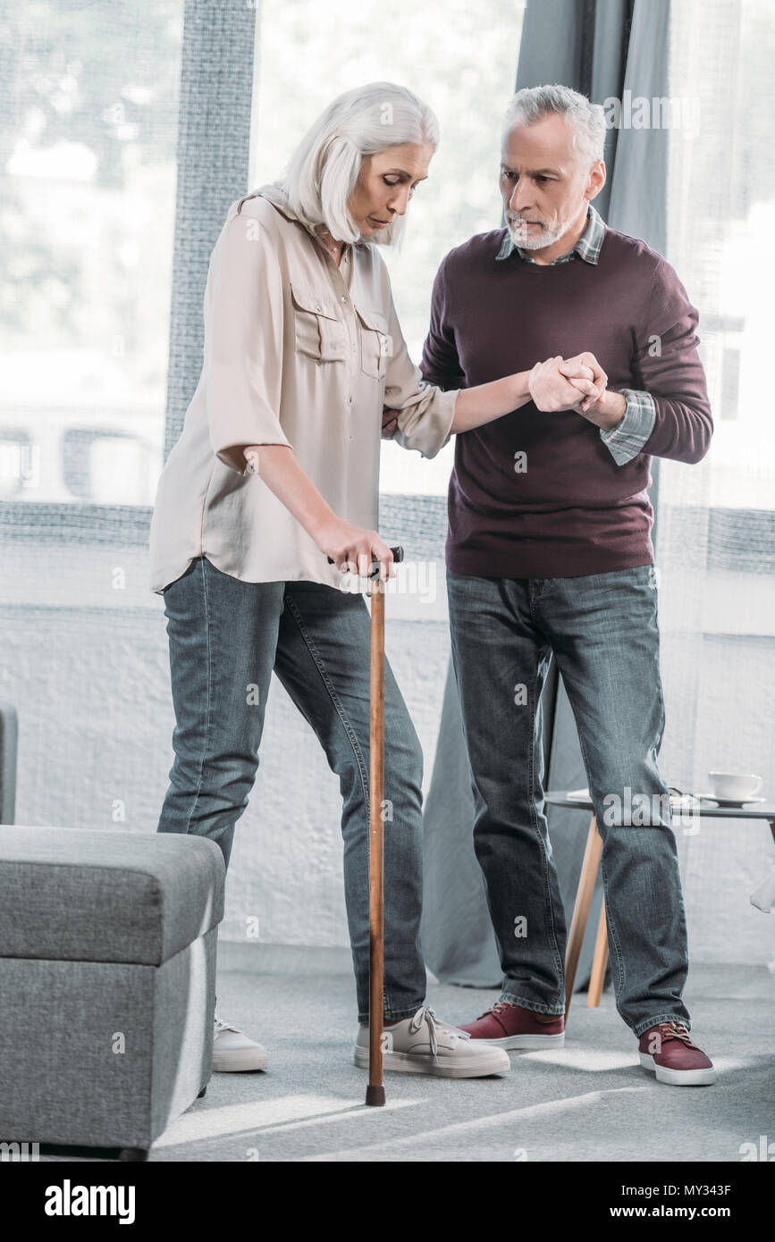 man helping senior wife with walking stick to walk at home Stock Photo ...