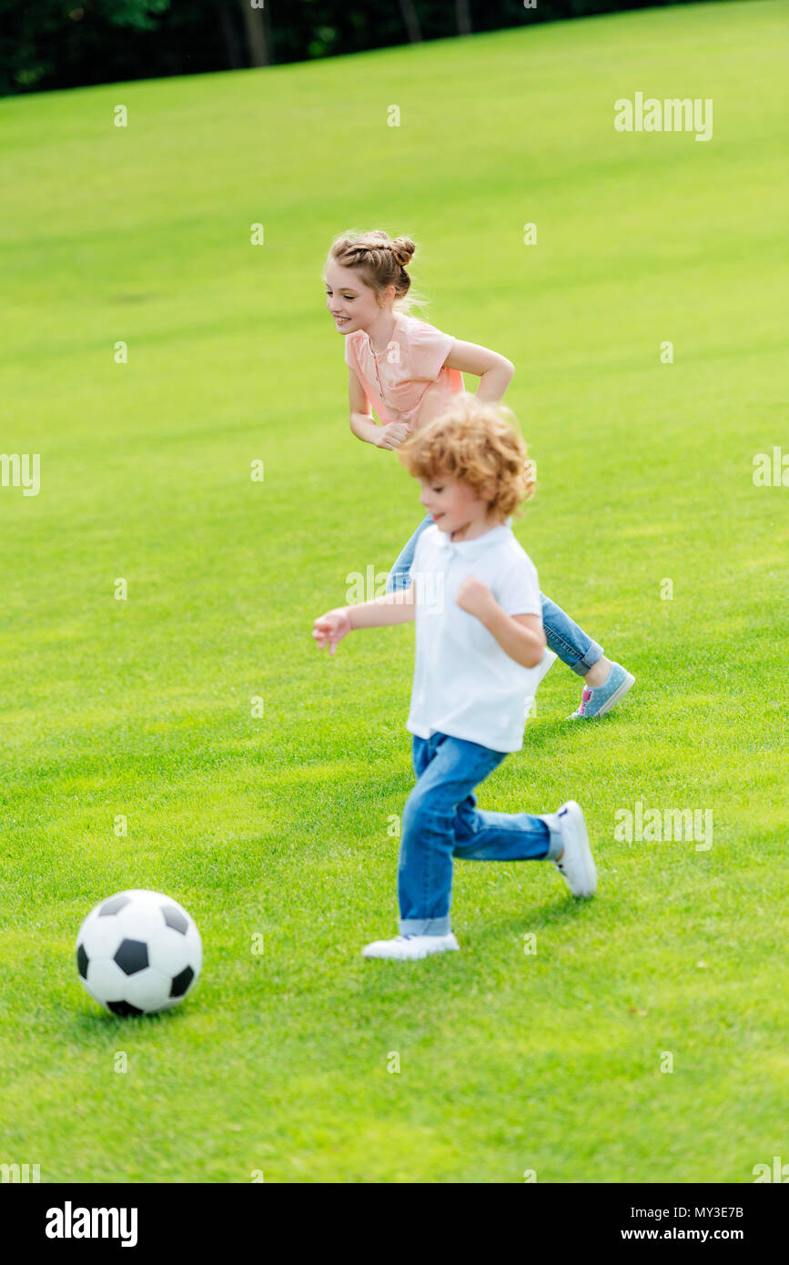 cute little brother and sister playing soccer on green grass in park ...