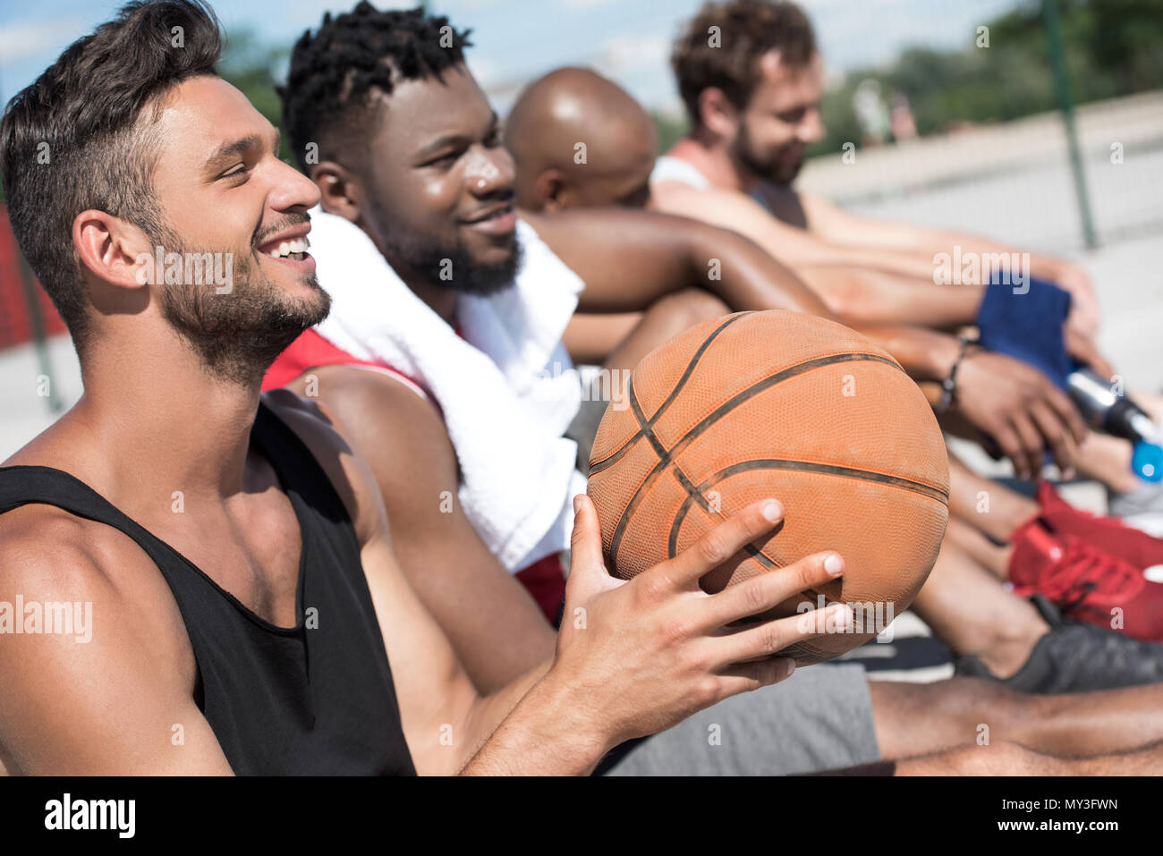 side view of multicultural basketball team resting after game on court ...