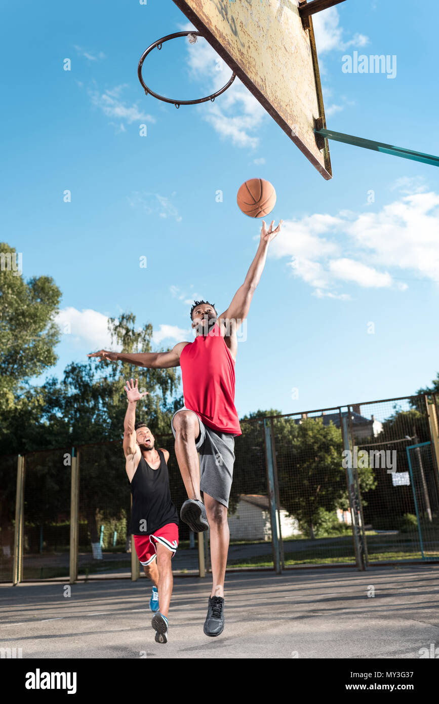 handsome multicultural basketball players playing basketball on court ...