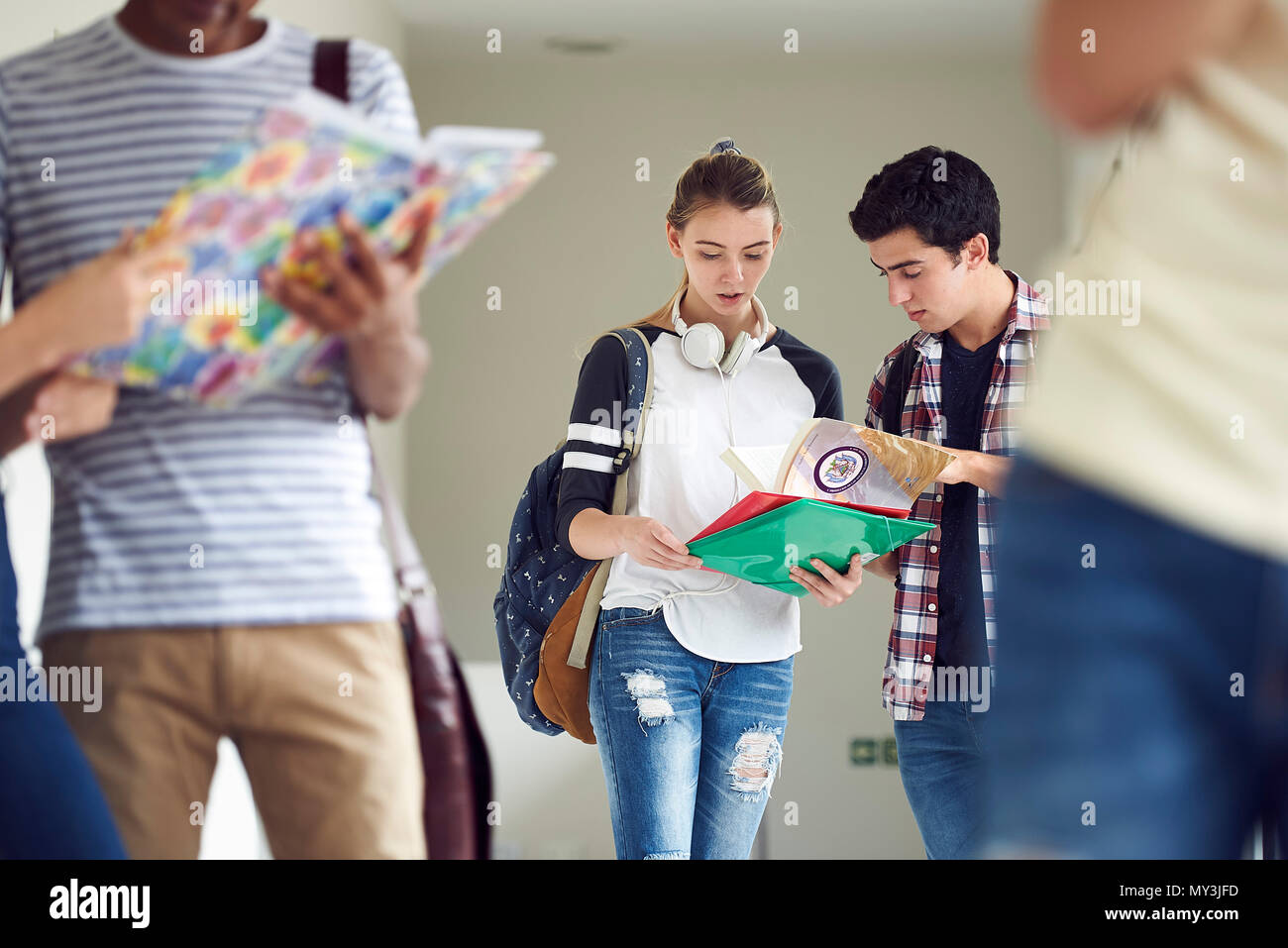 Classmates looking at textbook together in corridor Stock Photo - Alamy