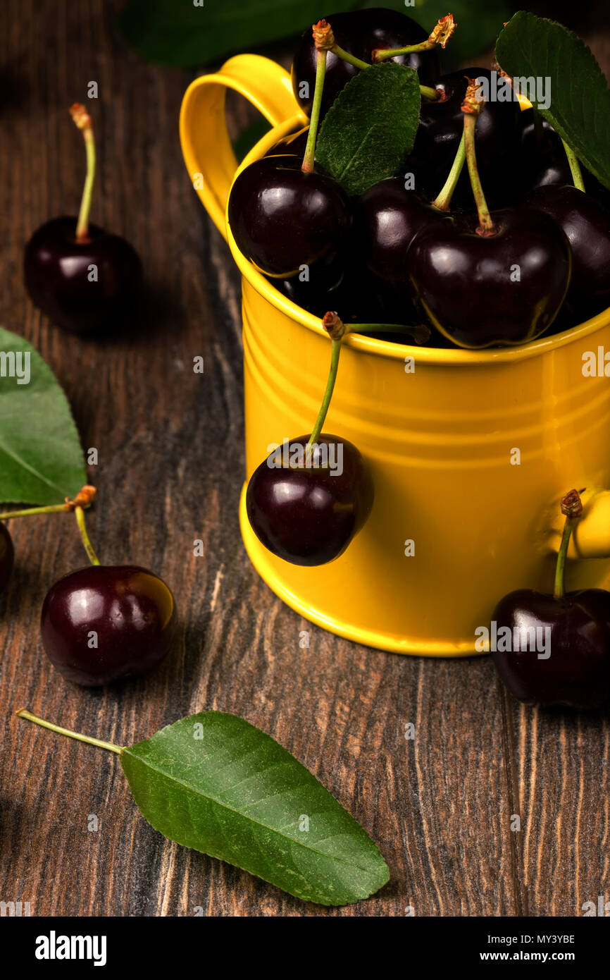 Black cherries in a yellow garden watering container Stock Photo - Alamy