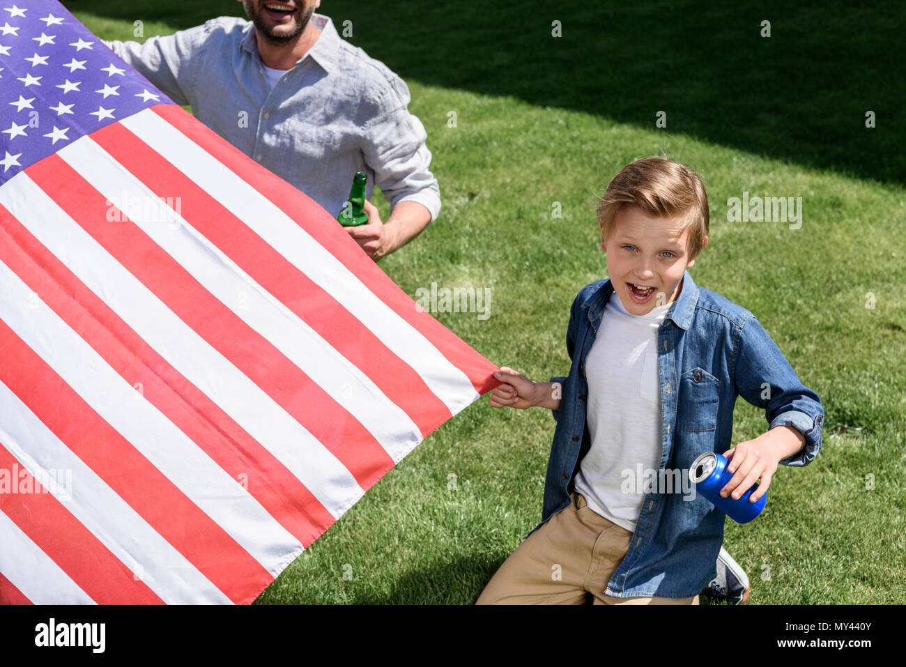 father and son sitting on grass with us flag and holding drinks ...