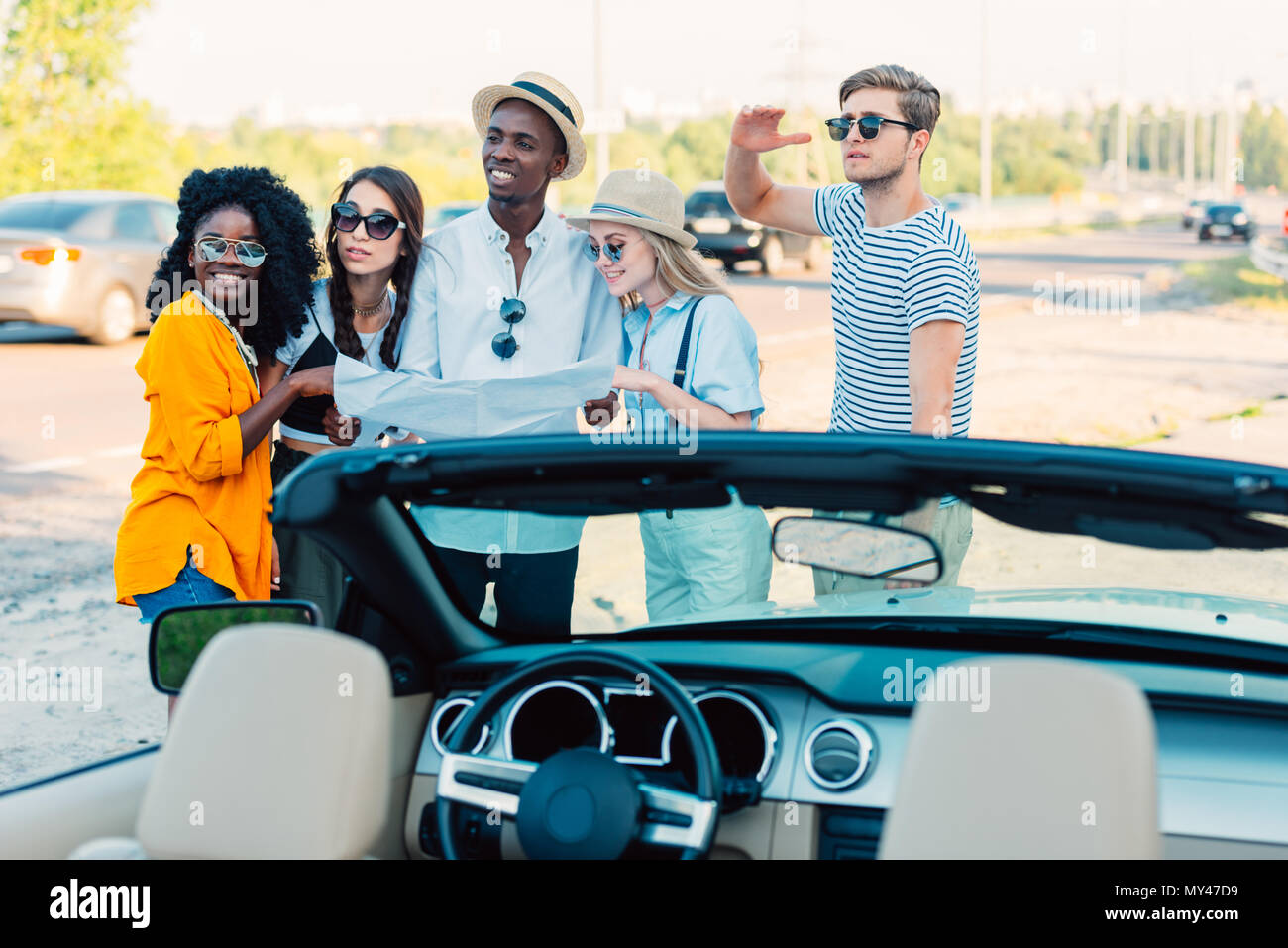 multiethnic group of friends use map to determine direction while ...