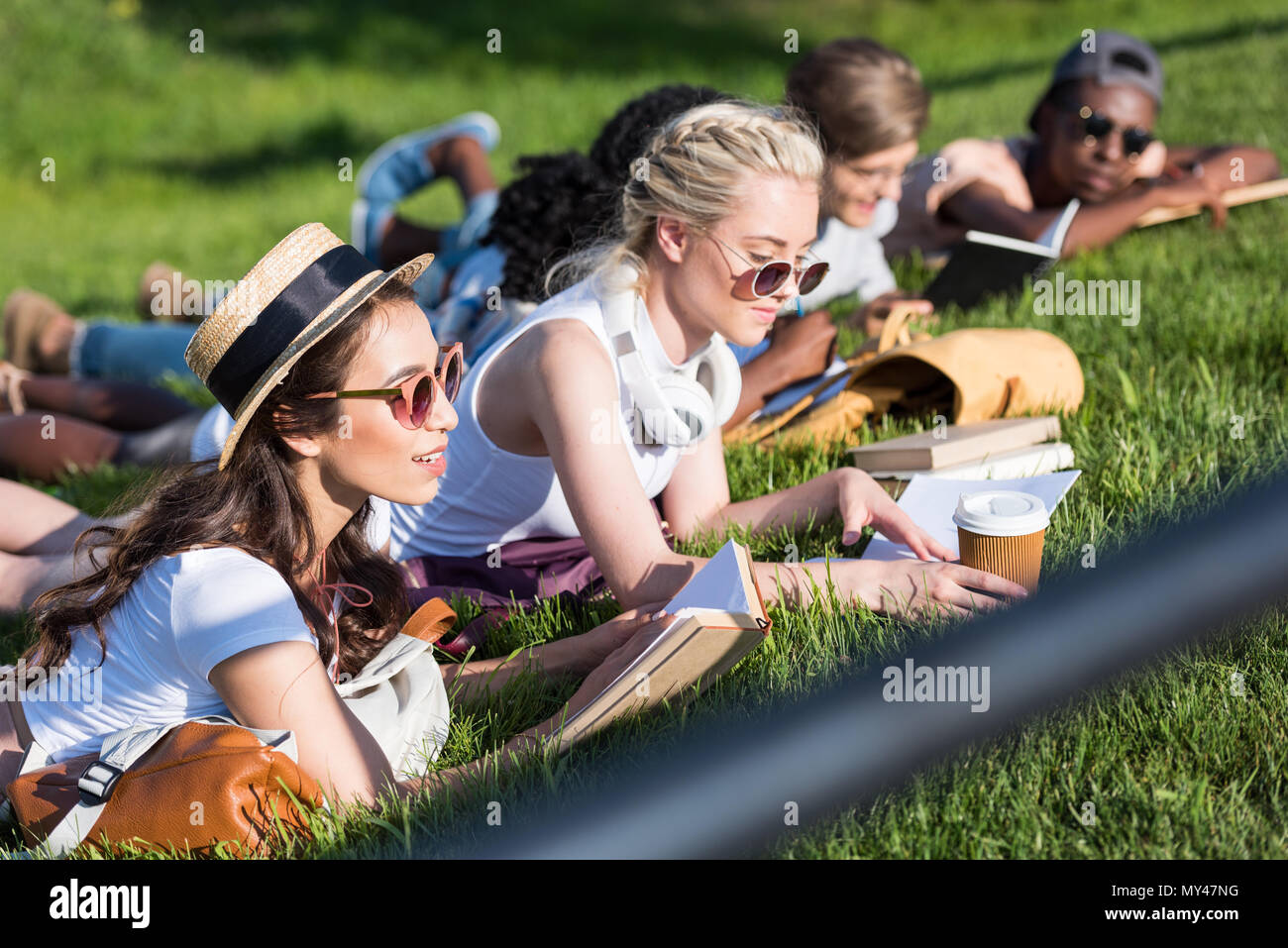 beautiful multiethnic girls reading books while lying on grass and ...