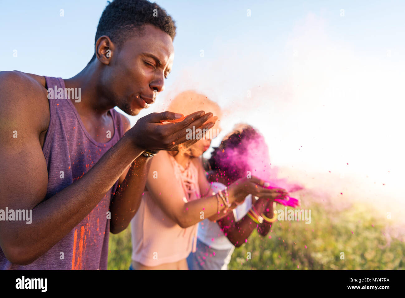 young multiethnic people blowing colorful powder from palms at holi ...