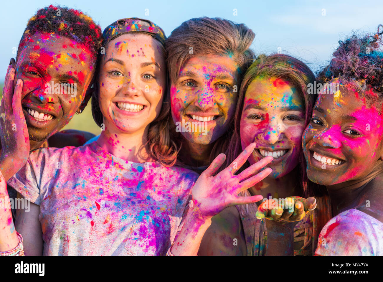 happy young multiethnic friends having fun with colorful powder at holi ...