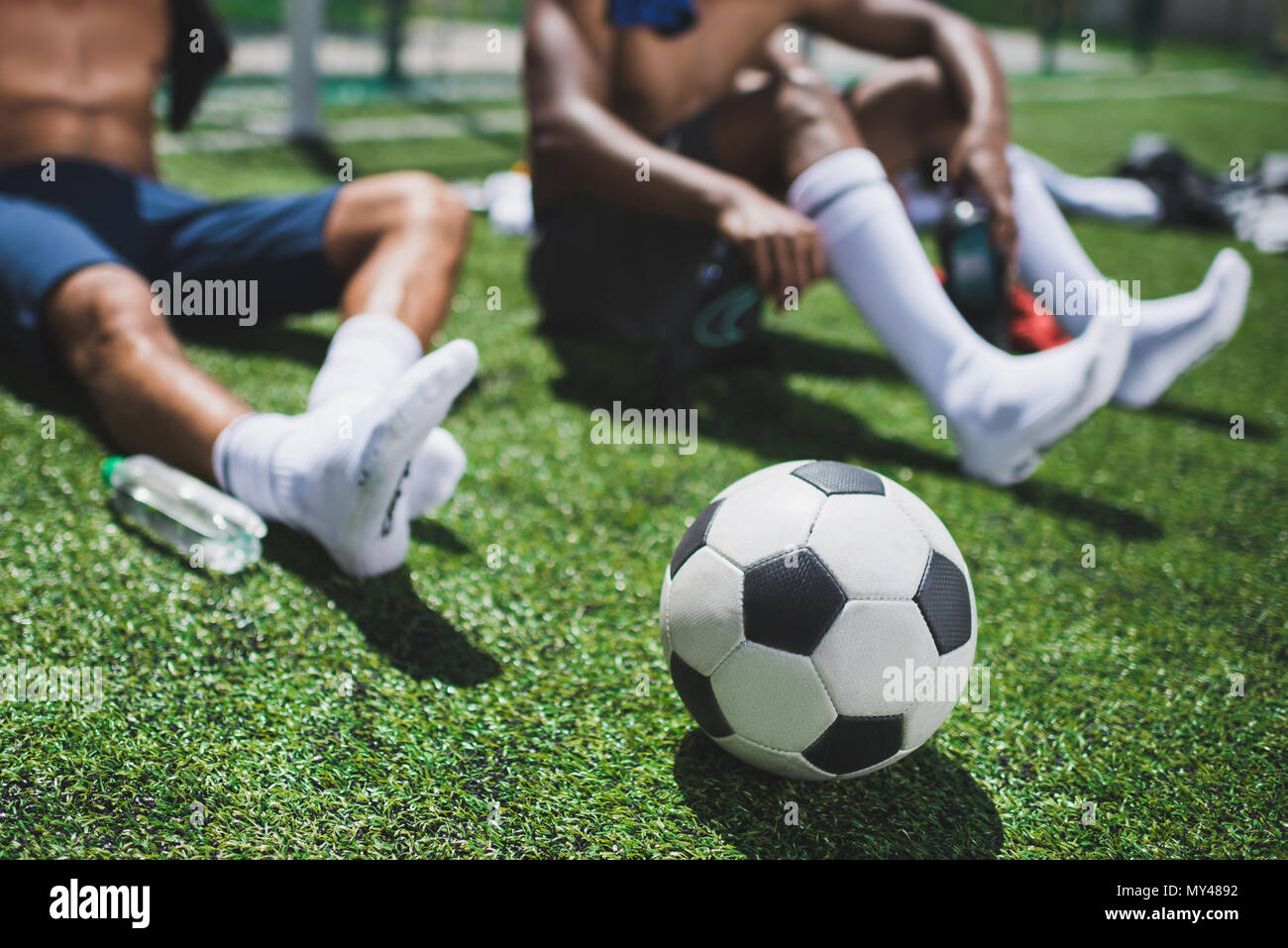 soccer players resting on football field with soccer ball on foreground ...
