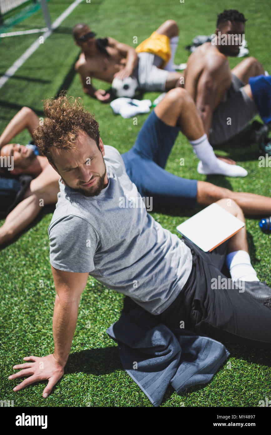 group of multiethnic soccer players resting on football field after ...