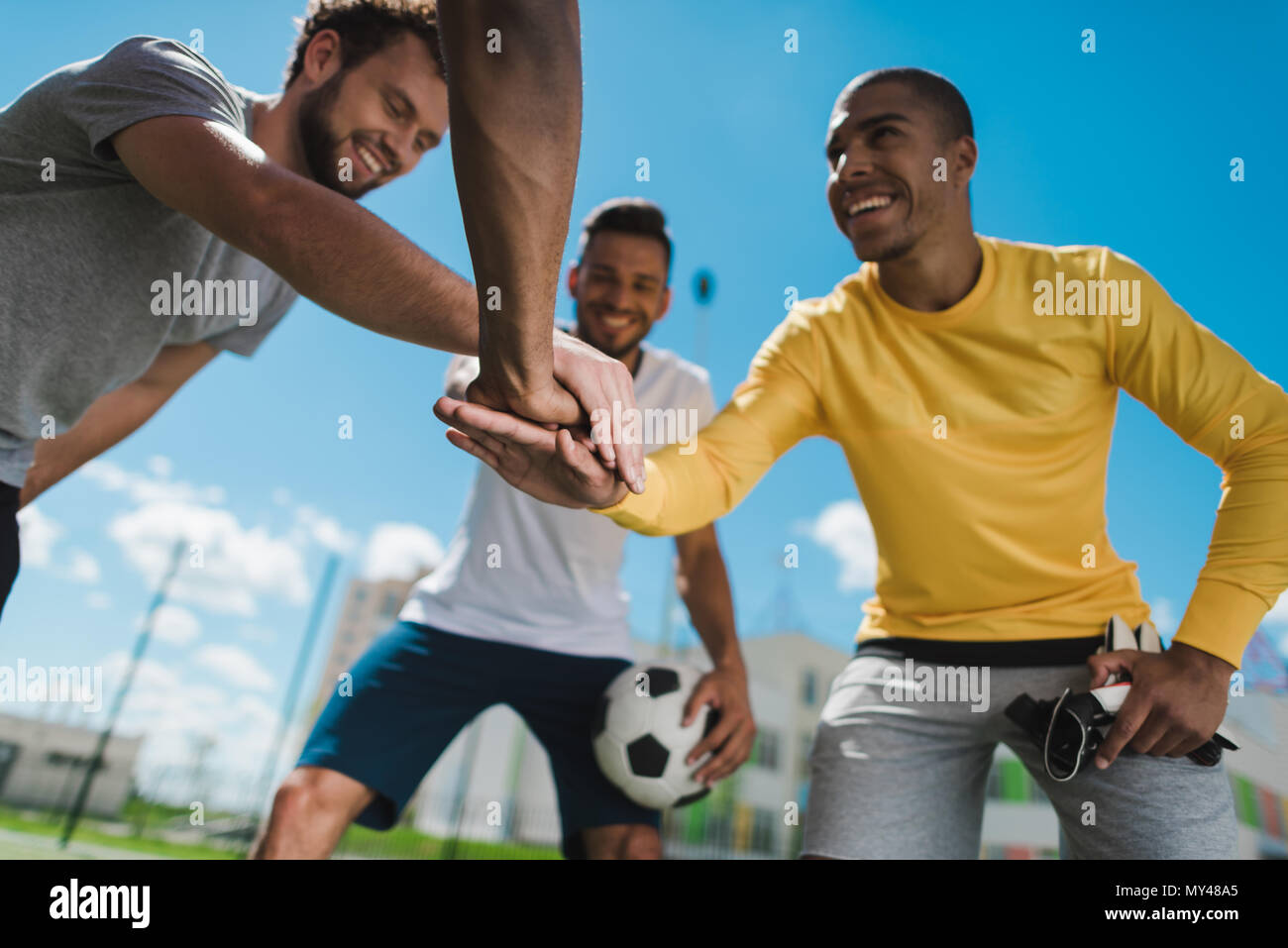 Low angle view of happy multiethnic soccer team holding hands together ...