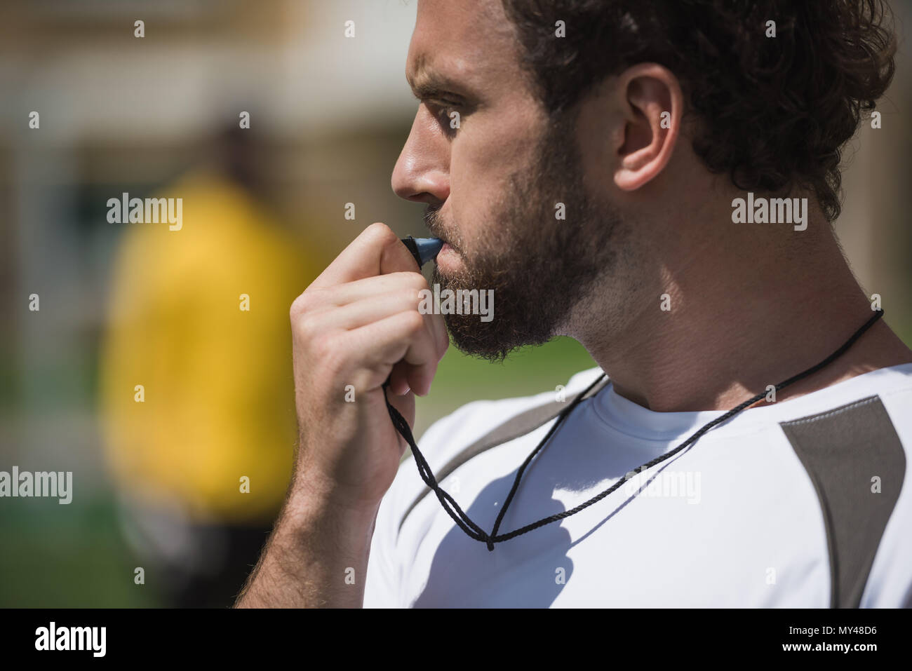 side view of soccer referee whistling in whistle on soccer pitch during ...
