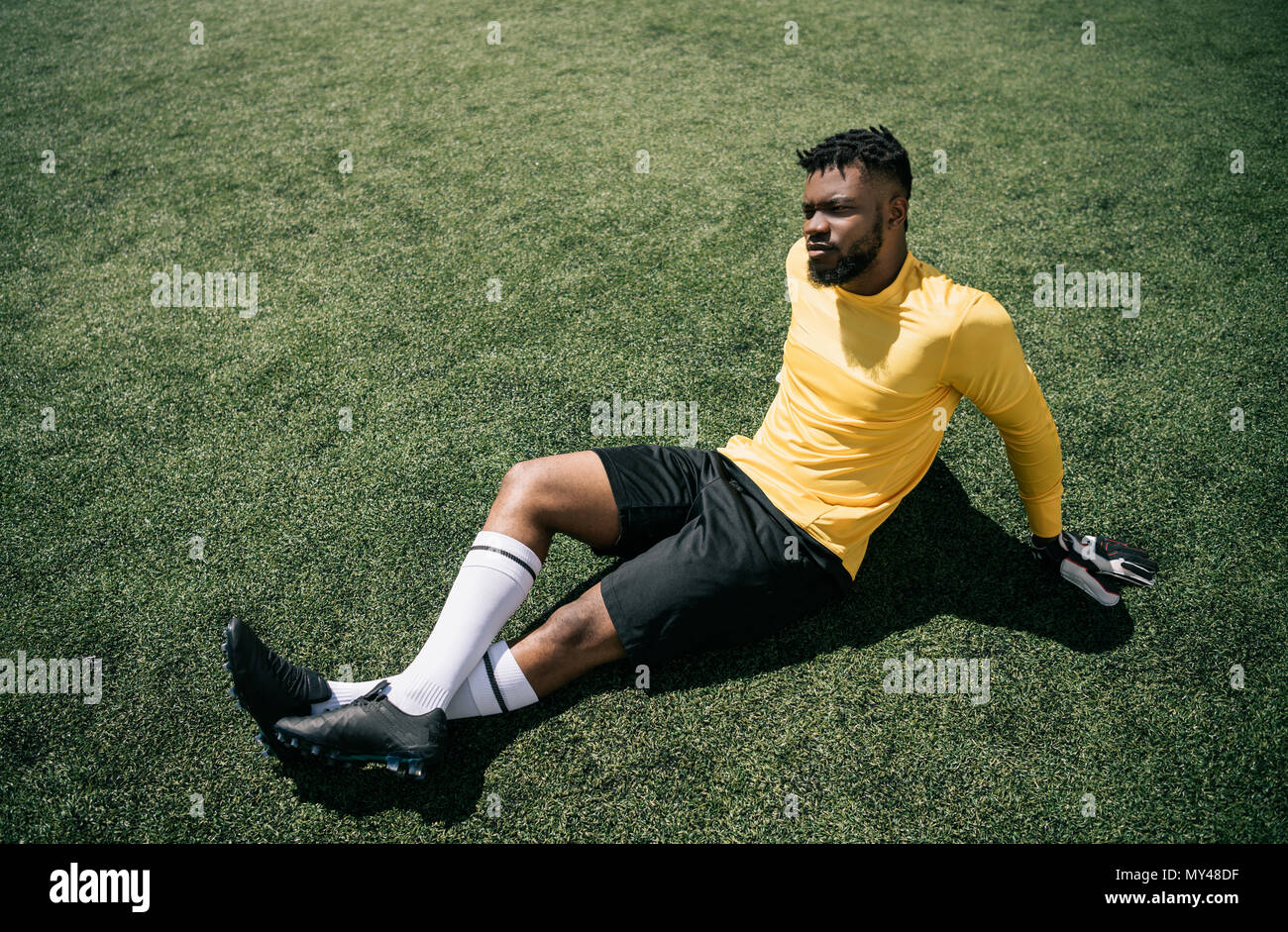athletic african american goalkeeper sitting on soccer pitch Stock ...