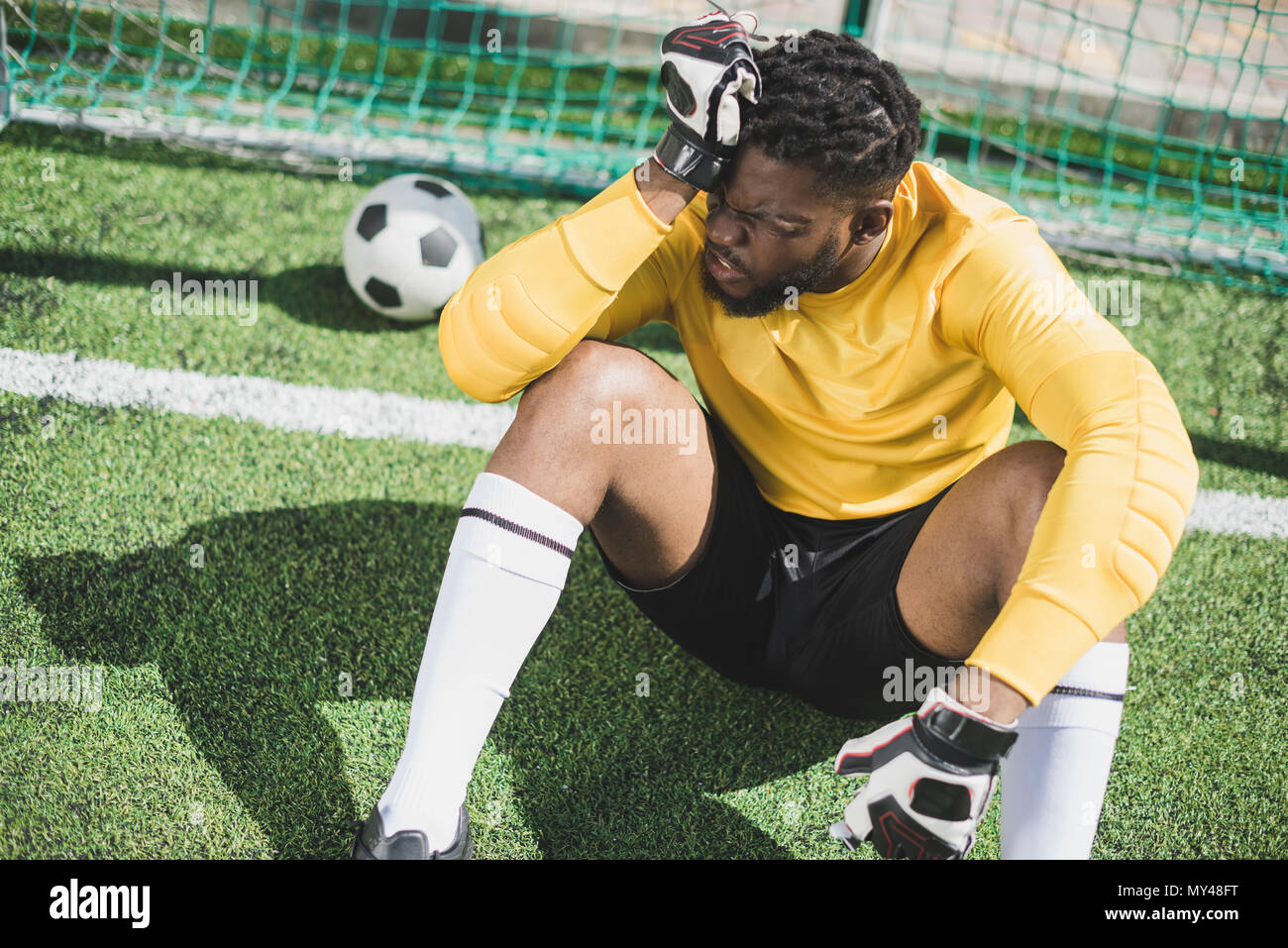 upset african american goalkeeper sitting at goalpost on pitch Stock ...