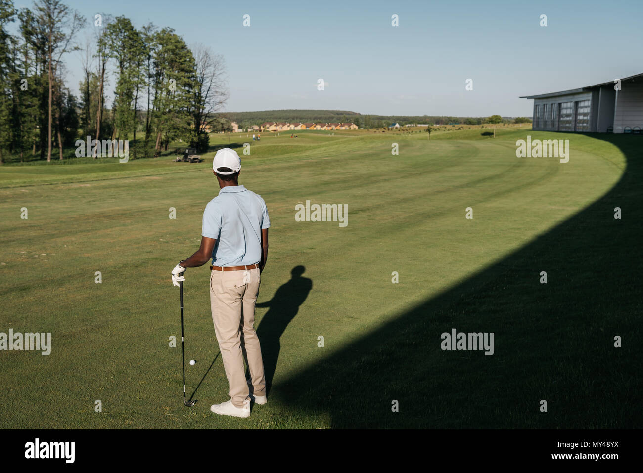 Back view of african american man playing golf with club and ball at ...