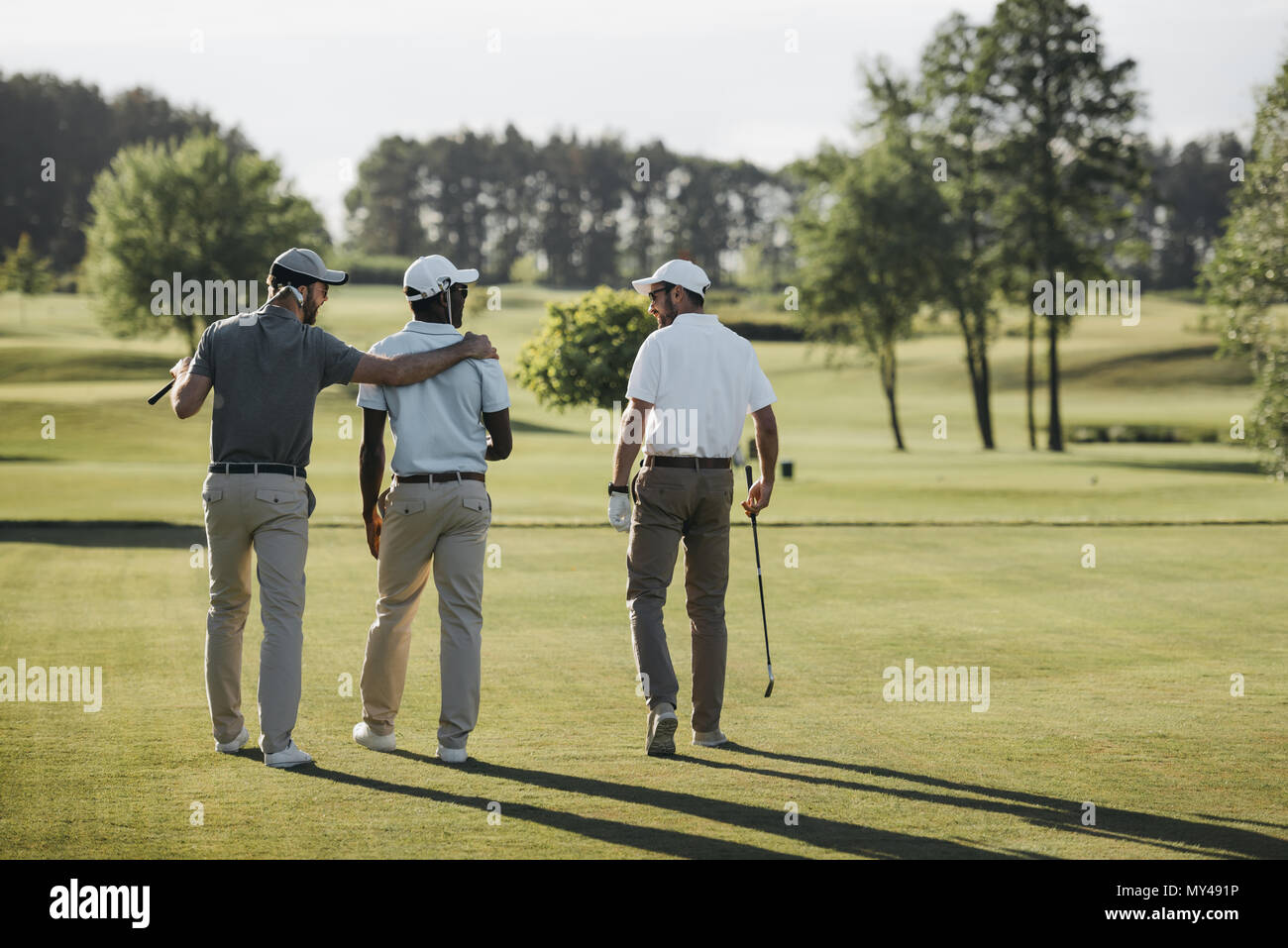 back view of multiethnic golf players hugging and walking on golf ...