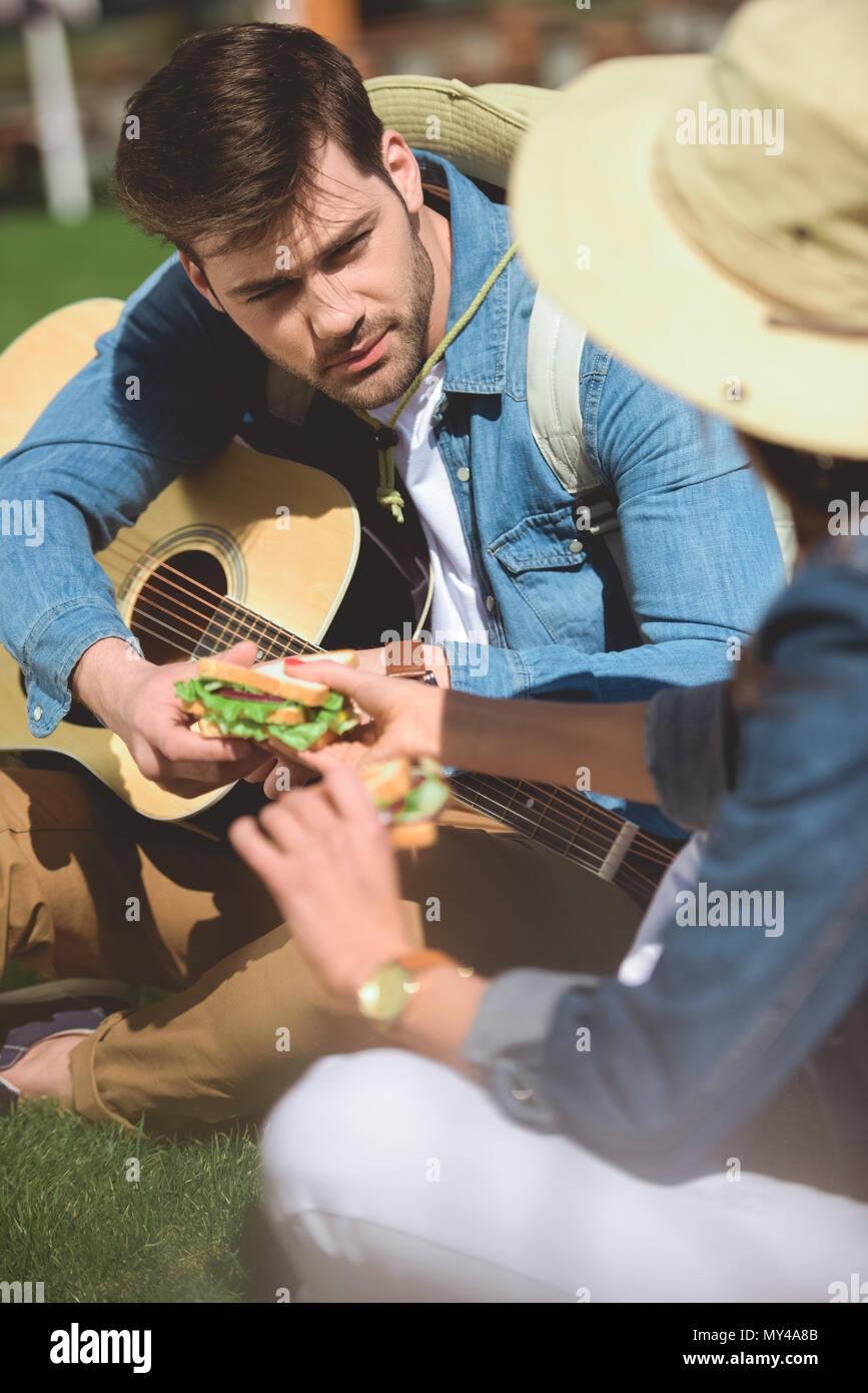 rear view of stylish female tourist giving sandwich to boyfriend with ...