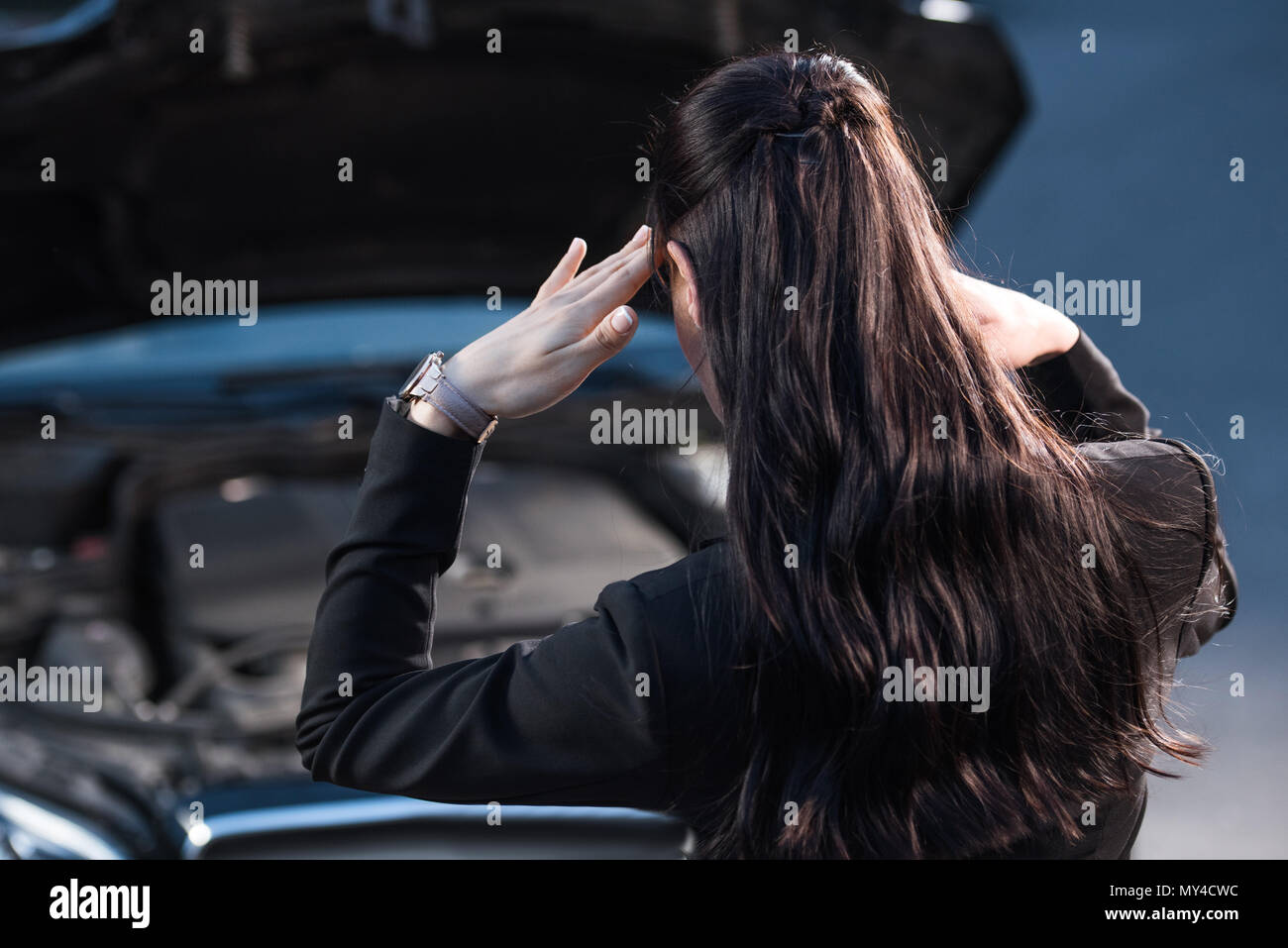 Young troubled woman rubbing temples while looking under hood of broken car Stock Photo - Alamy