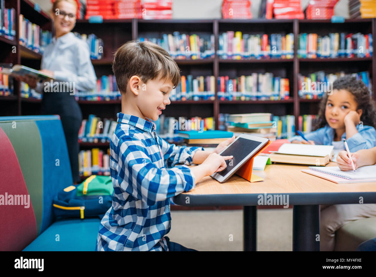 cute smiling schoolboy using tablet at library Stock Photo - Alamy