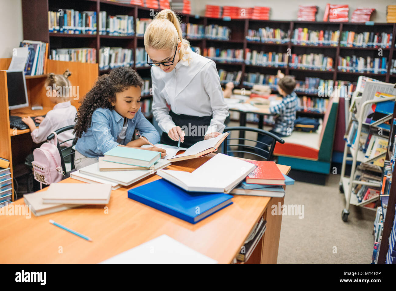 young teacher helping schoolgirl with homework in library Stock Photo ...