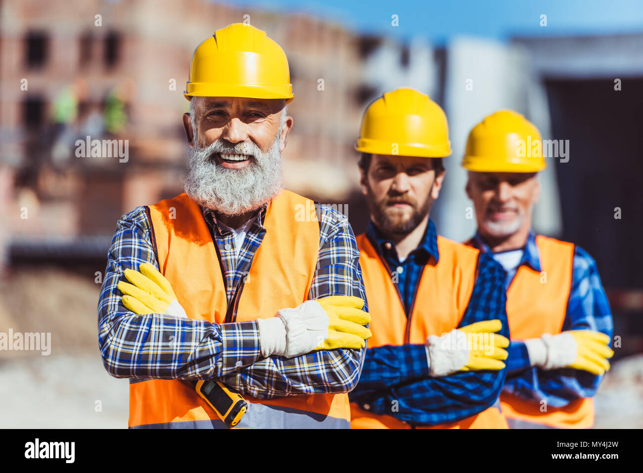 Three labour workers posing with arms crossed at the construction site ...
