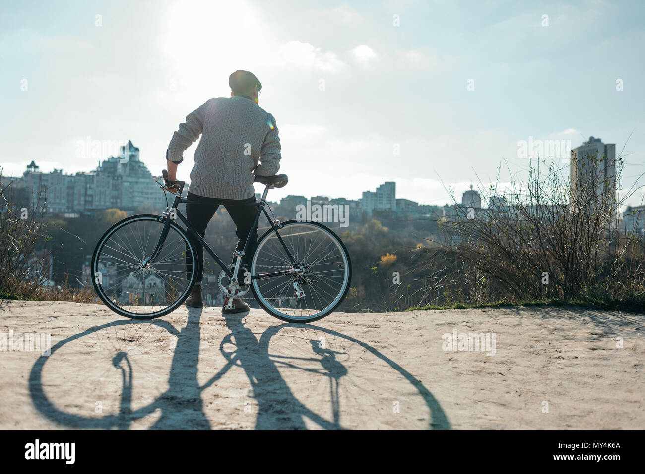 back view of stylish man sitting on bicycle and looking at city Stock ...