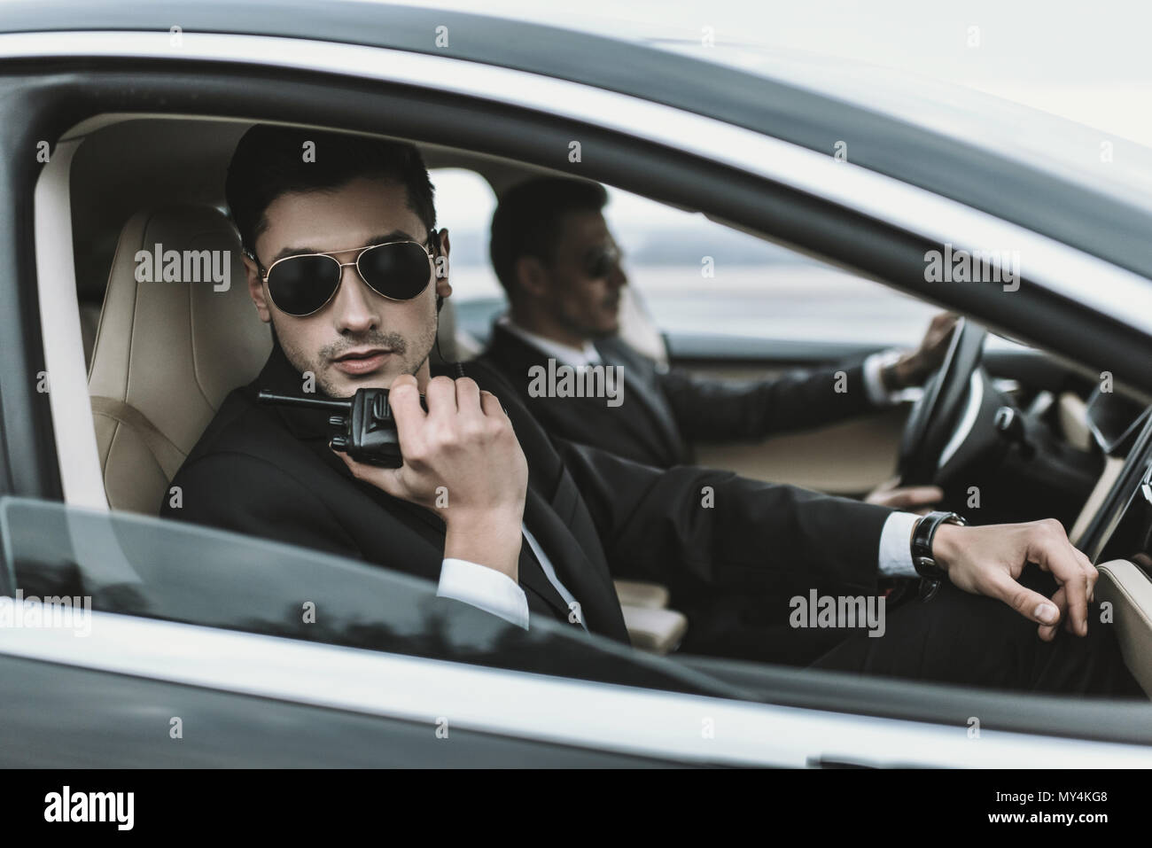 bodyguard in sunglasses talking by portable radio while sitting in car ...