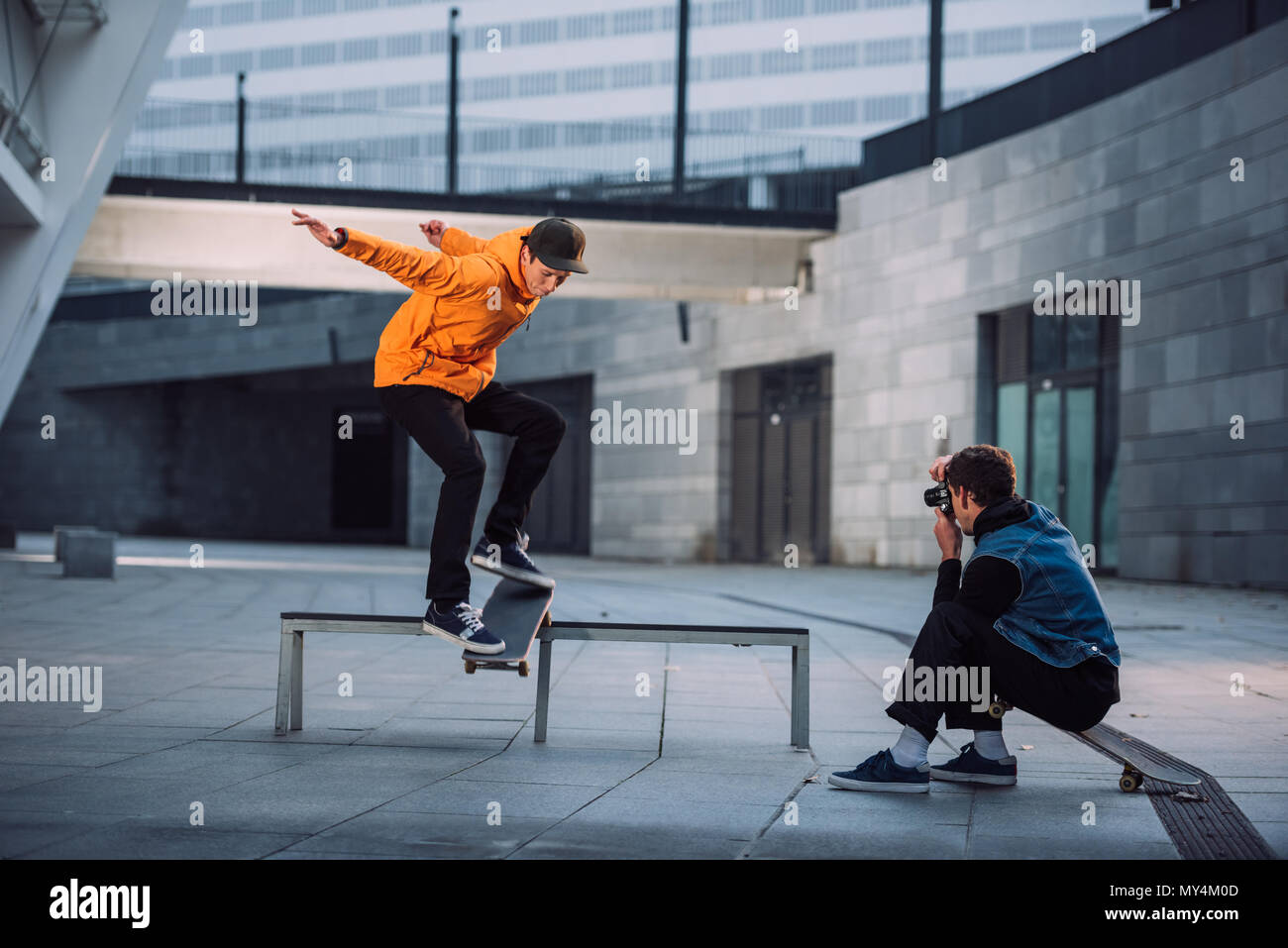 man taking photo of skateboarder jumping over bench in urban location ...