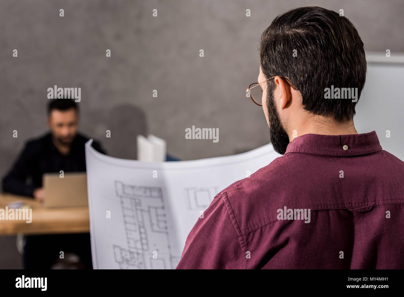 rear view of architect looking at blueprint in office Stock Photo - Alamy