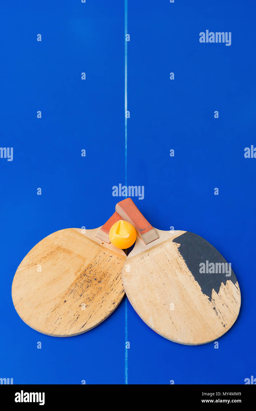 pair of old pingpong rackets and a dented ball on a blue pingpong table ...