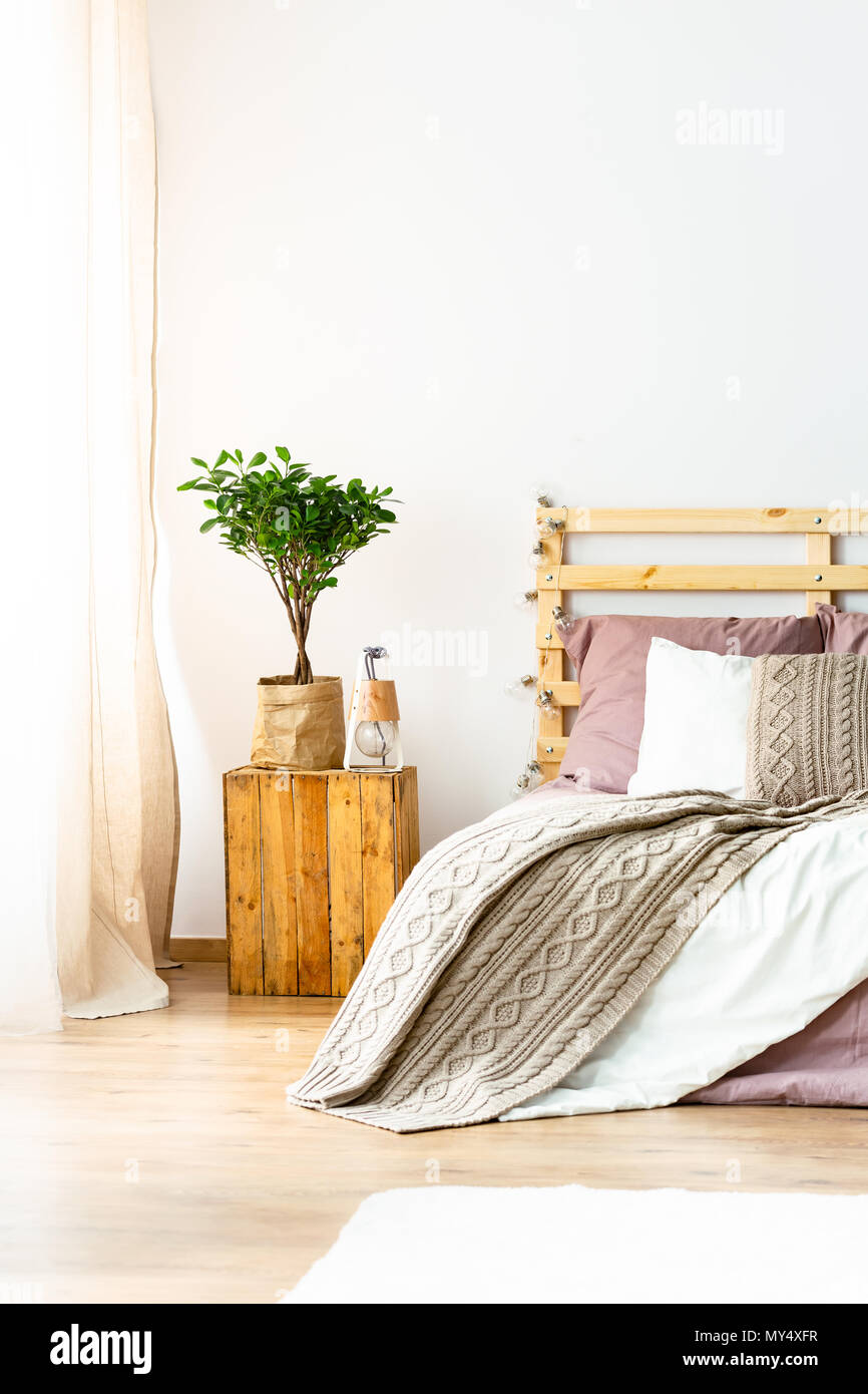 Plant on wooden stool next to bed with blanket in natural bedroom interior. Real photo Stock Photo Alamy