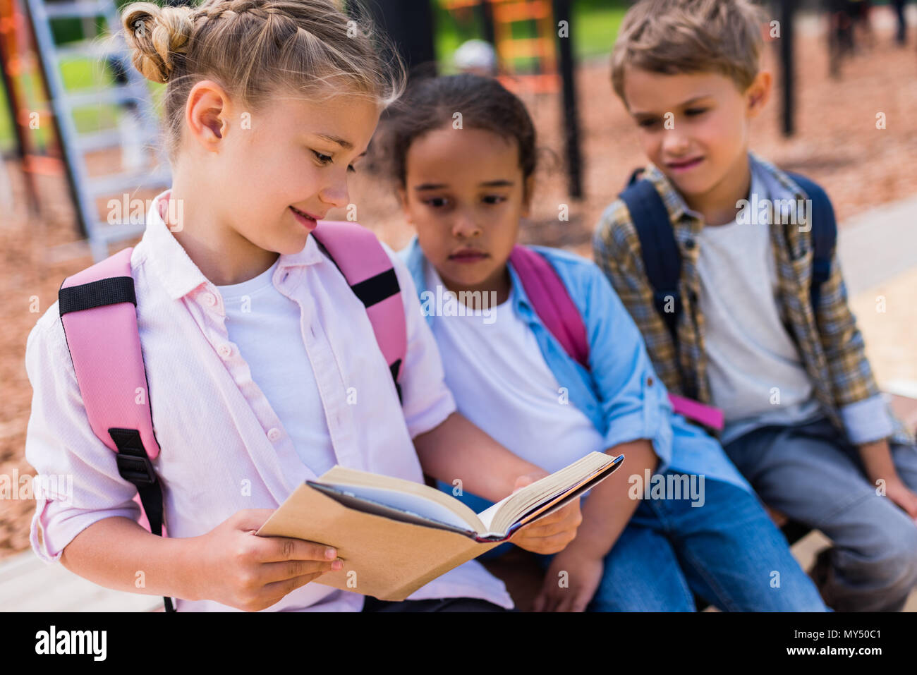 cute smiling multiethnic schoolkids with backpacks reading book ...