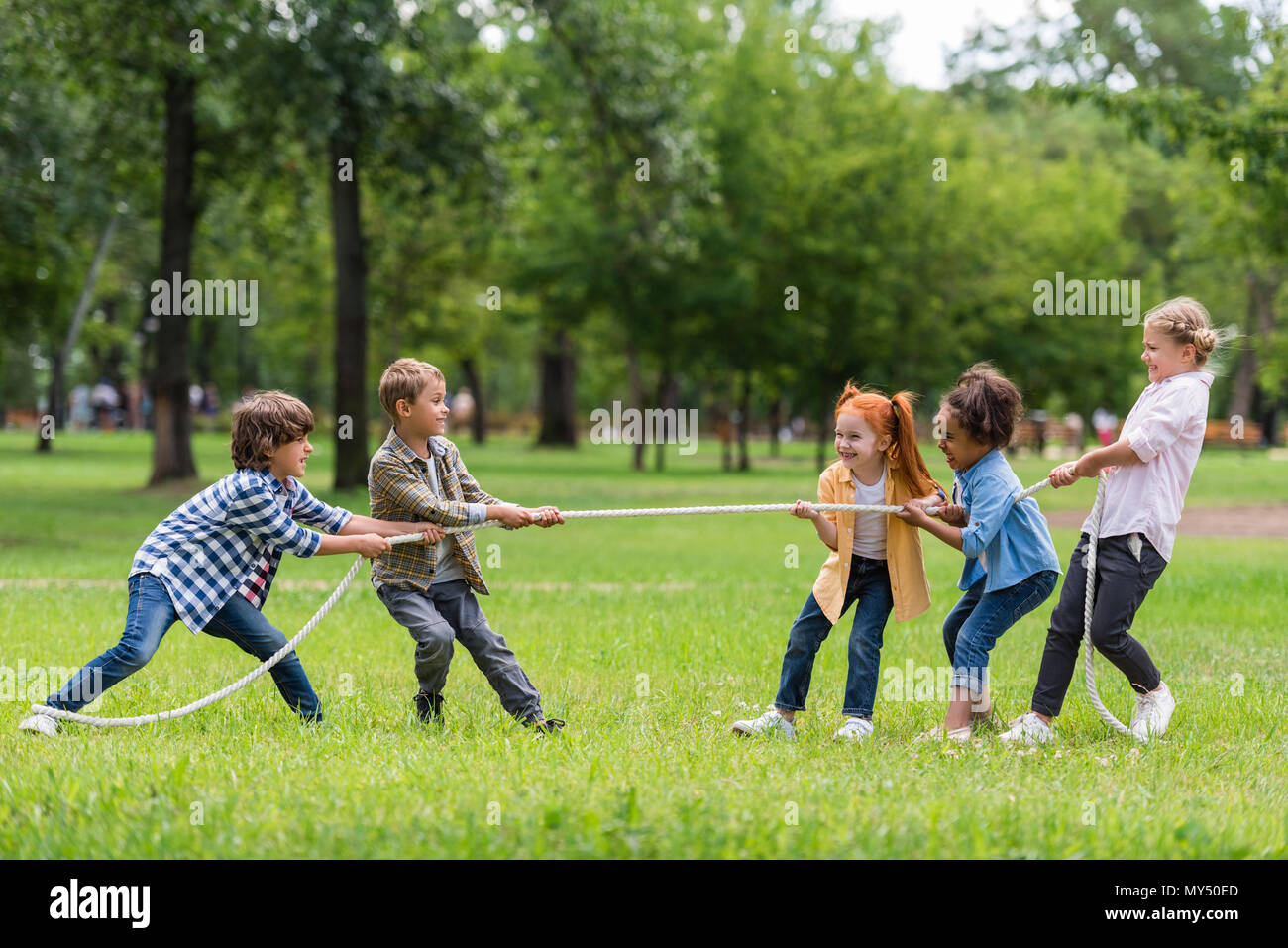 side view of cute little multiethnic children pulling rope in park ...