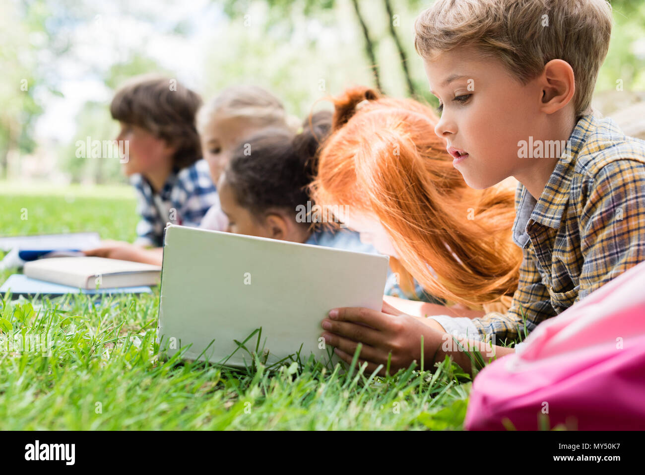 side view of cute little kids reading books while lying on grass in ...