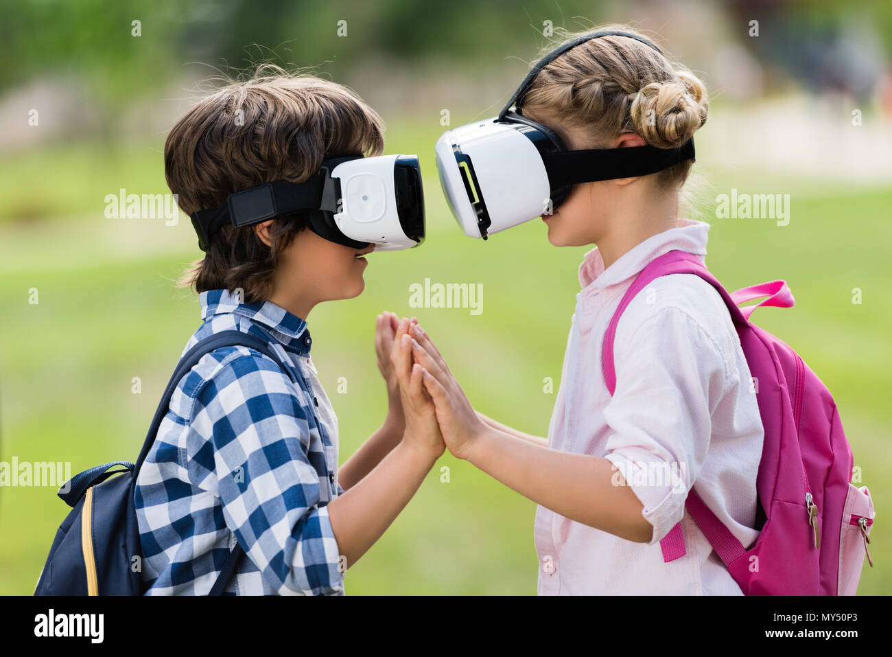 side view of cute smiling kids with backpacks using virtual reality ...