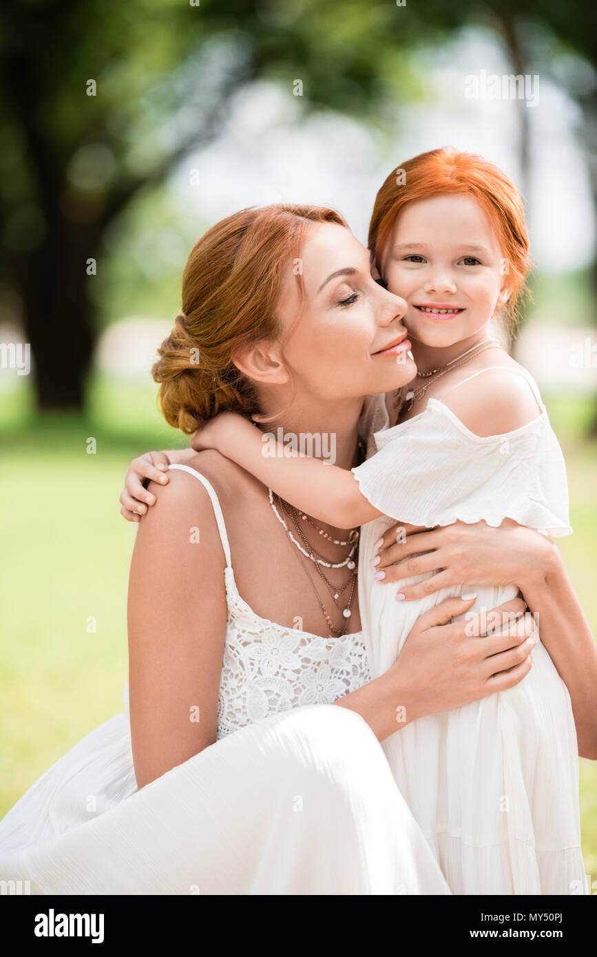 beautiful happy red haired mother and daughter in white dresses hugging at park Stock Photo - Alamy