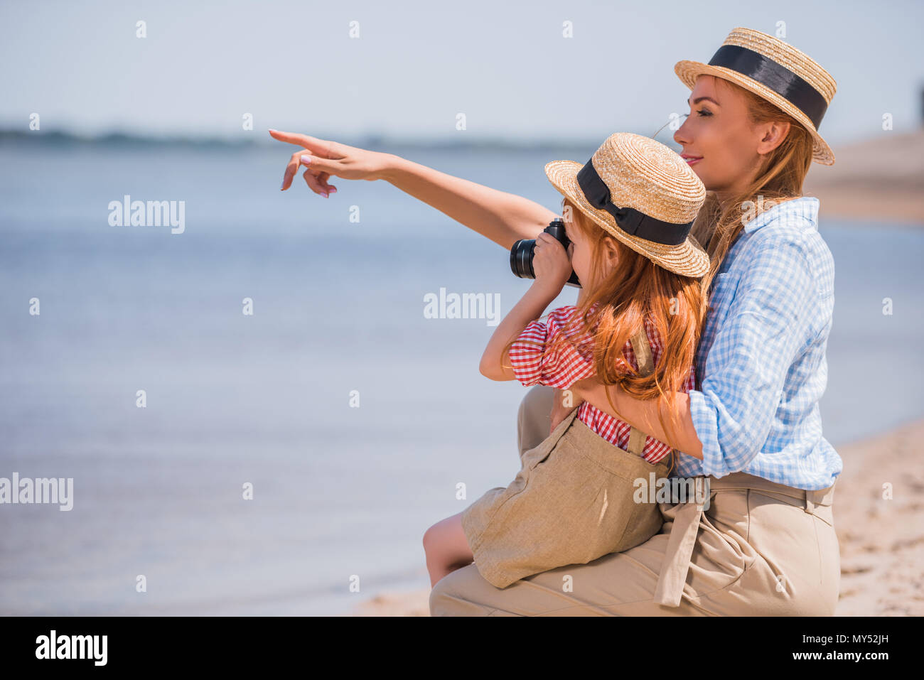 beautiful mother pointing with finger while daughter with camera ...
