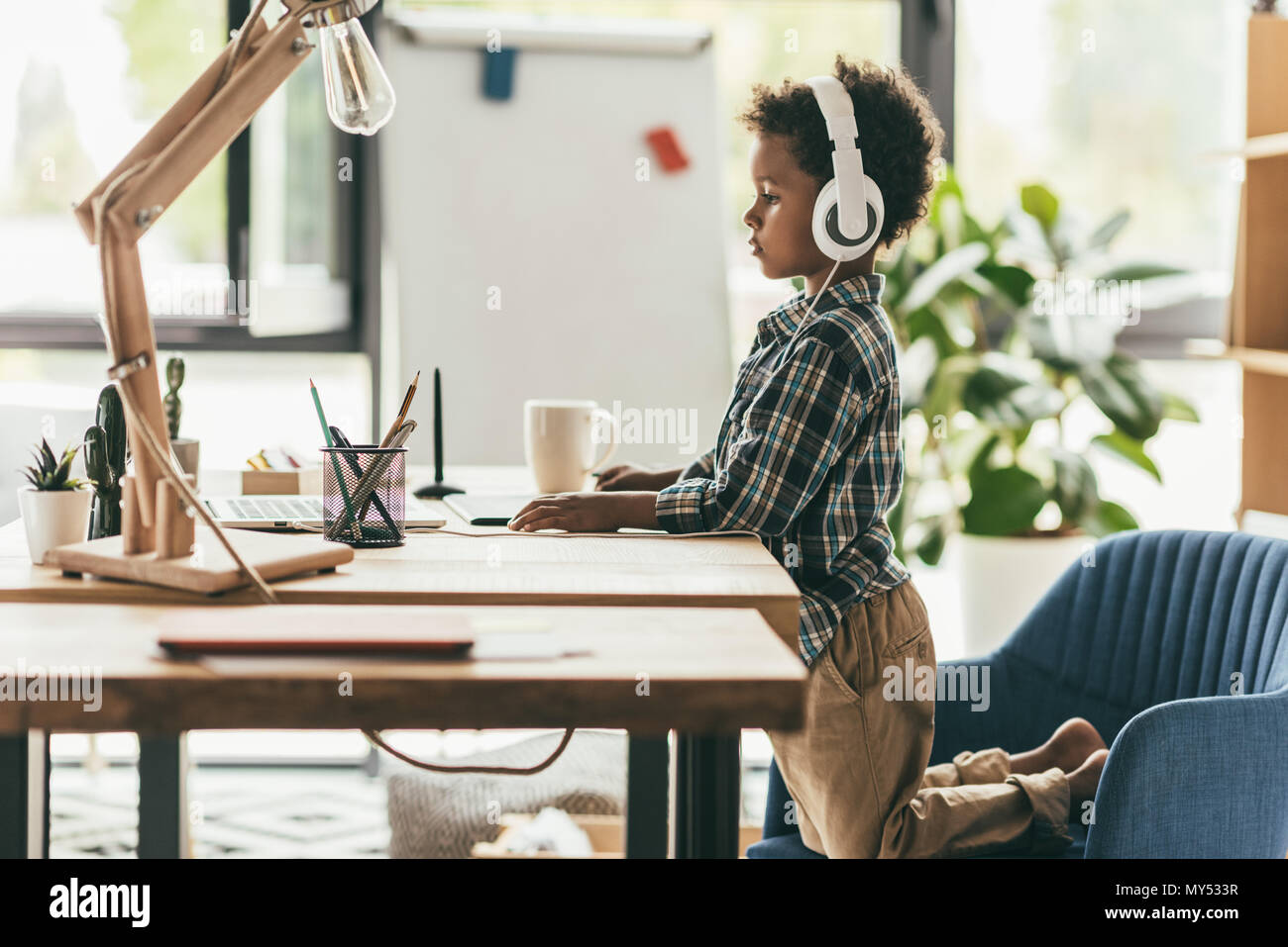 side view of little boy with headphones and cup looking at laptop Stock ...
