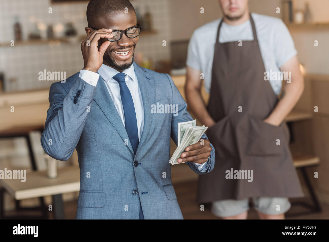 smiling african american businessman holding and counting money, waiter ...